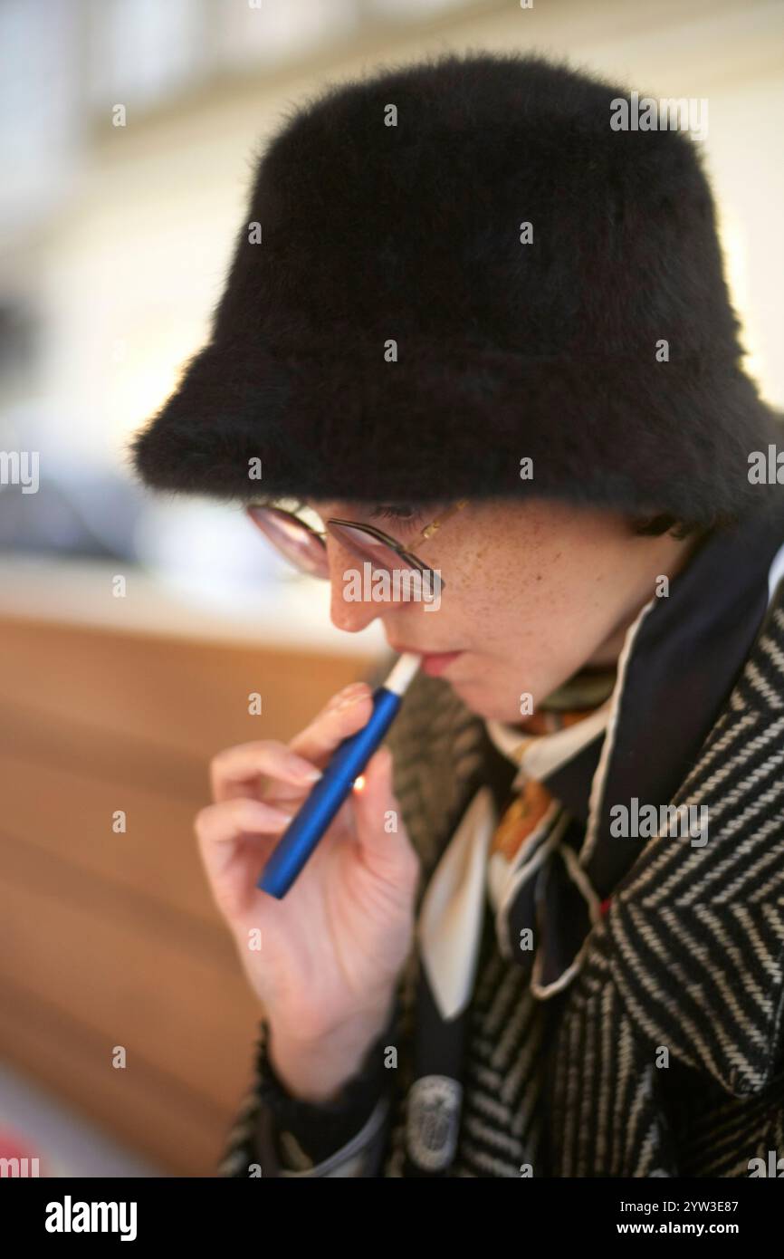 Young woman in a furry black hat and coat pensively vaping while ...