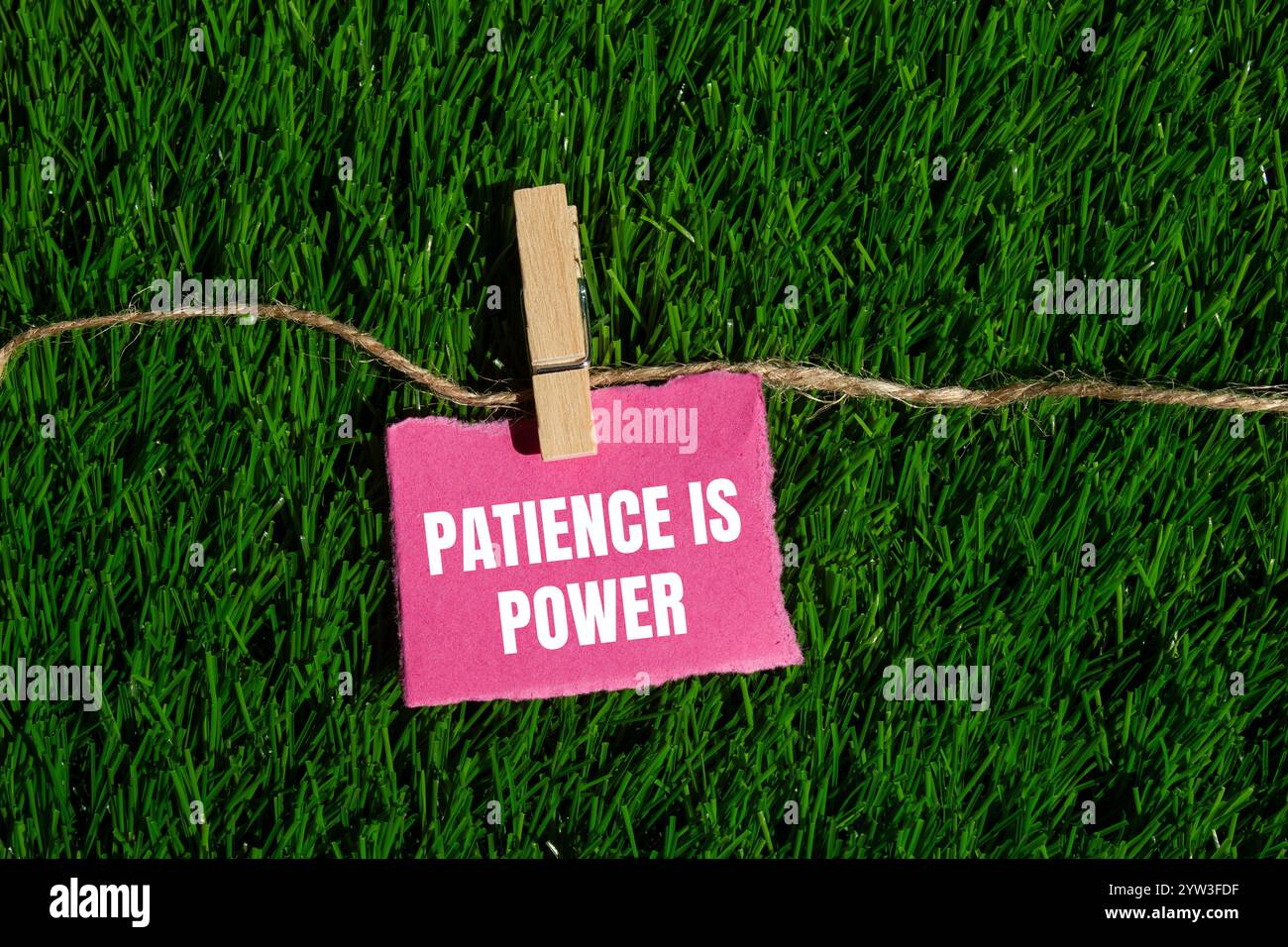 Patience is power message written on ripped torn pink paper piece with green grass background ...