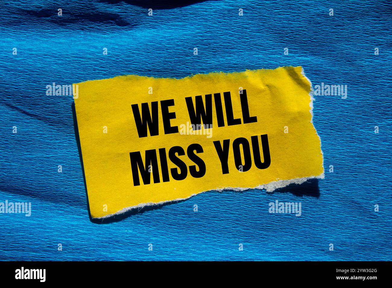 We will miss you message written on ripped torn yellow paper piece with blue background ...