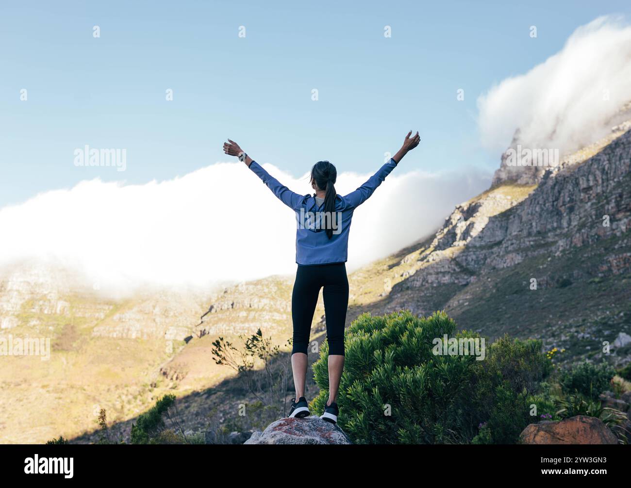 Back view of young slim female raising her hands in front of a mountain ...