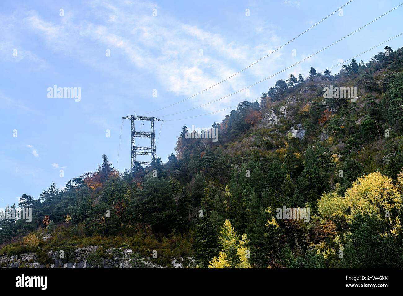 Metal tower with power lines on a forested mountain slope under a ...