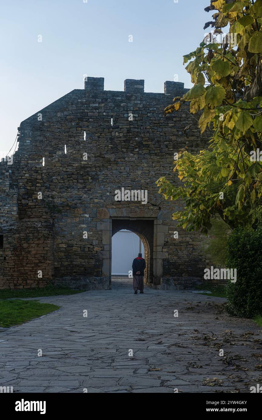 Historic stone wall with an arched gateway, surrounded by greenery, in ...