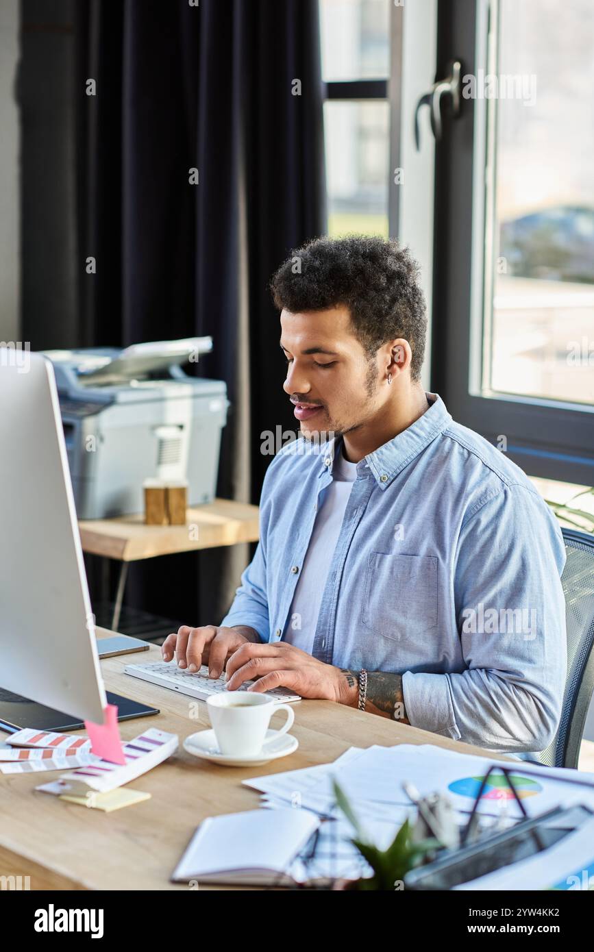 A handsome man types intently on his computer in a well lit workspace ...