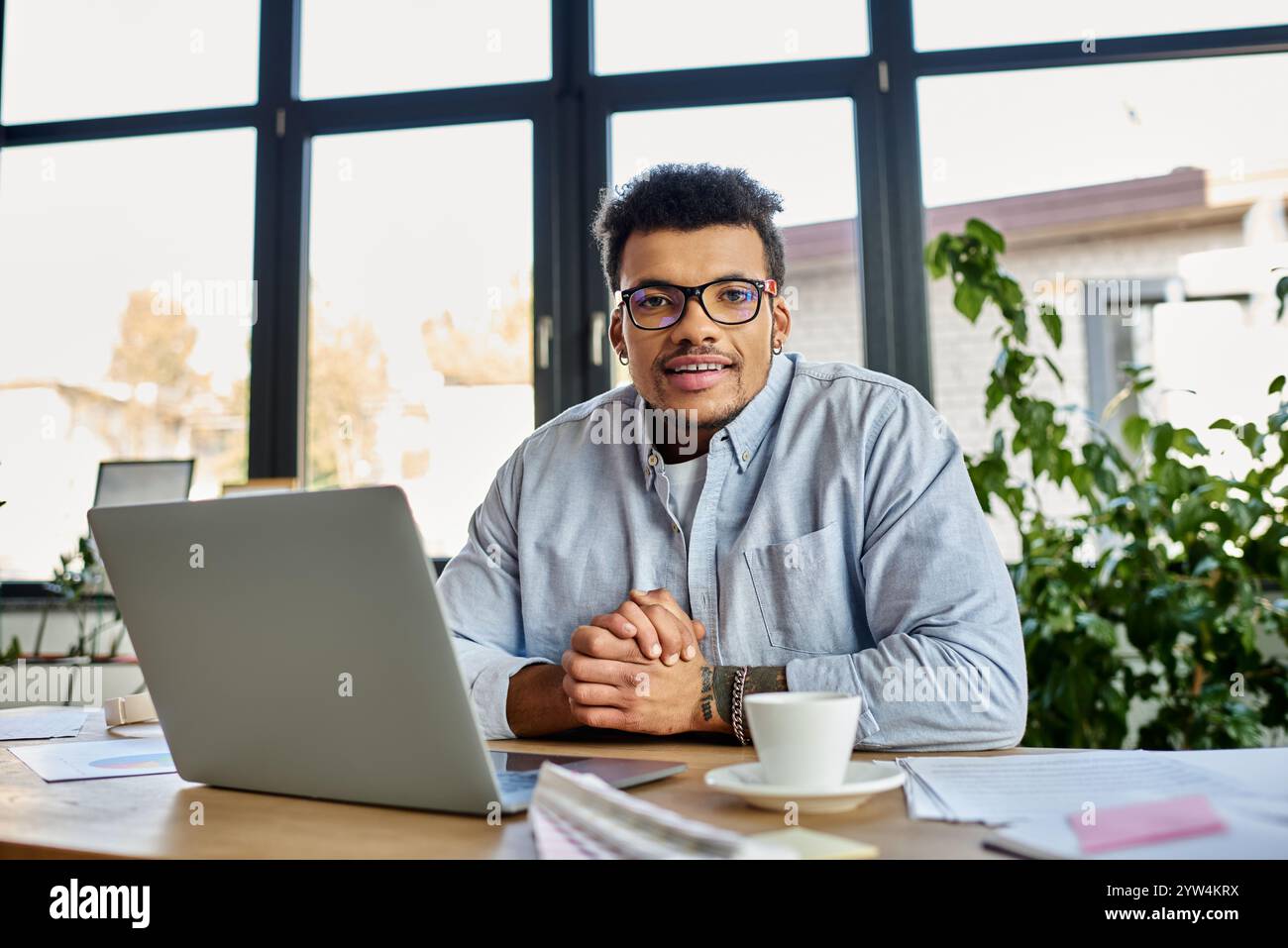 Friendly man smiles while working at his desk surrounded by greenery ...