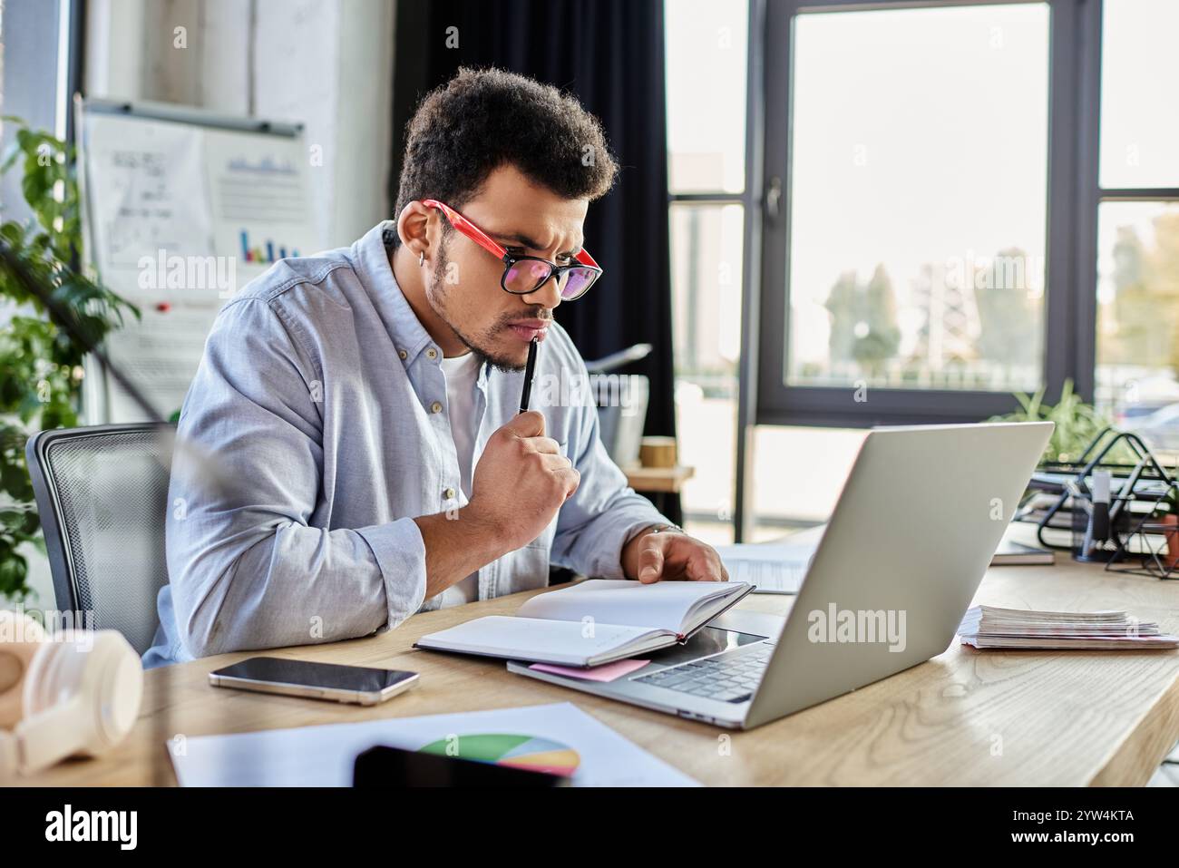 Concentrated man takes notes while working intently on a laptop in a ...