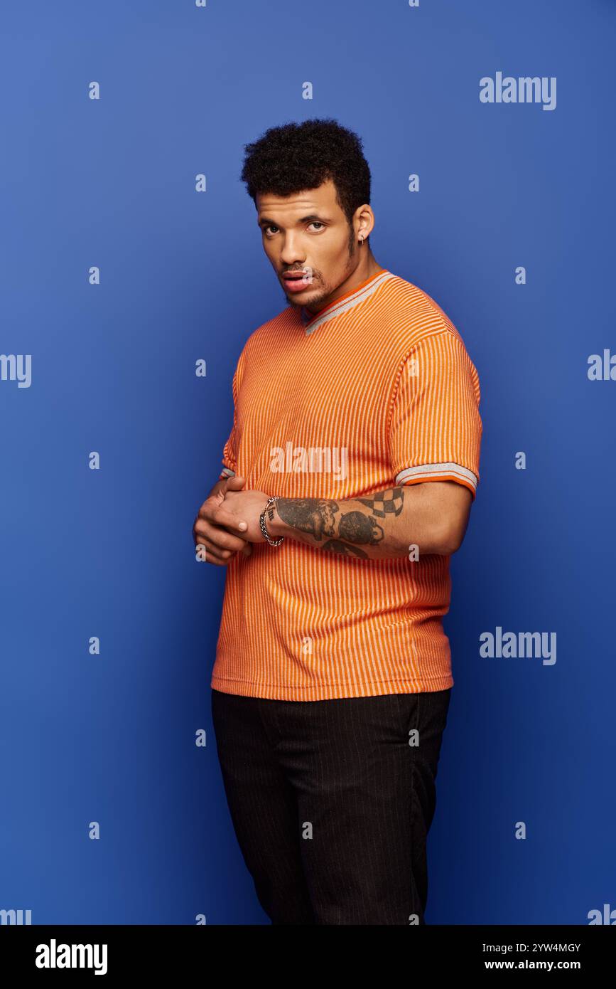 A stylish man with a strong presence poses against a bold blue wall ...