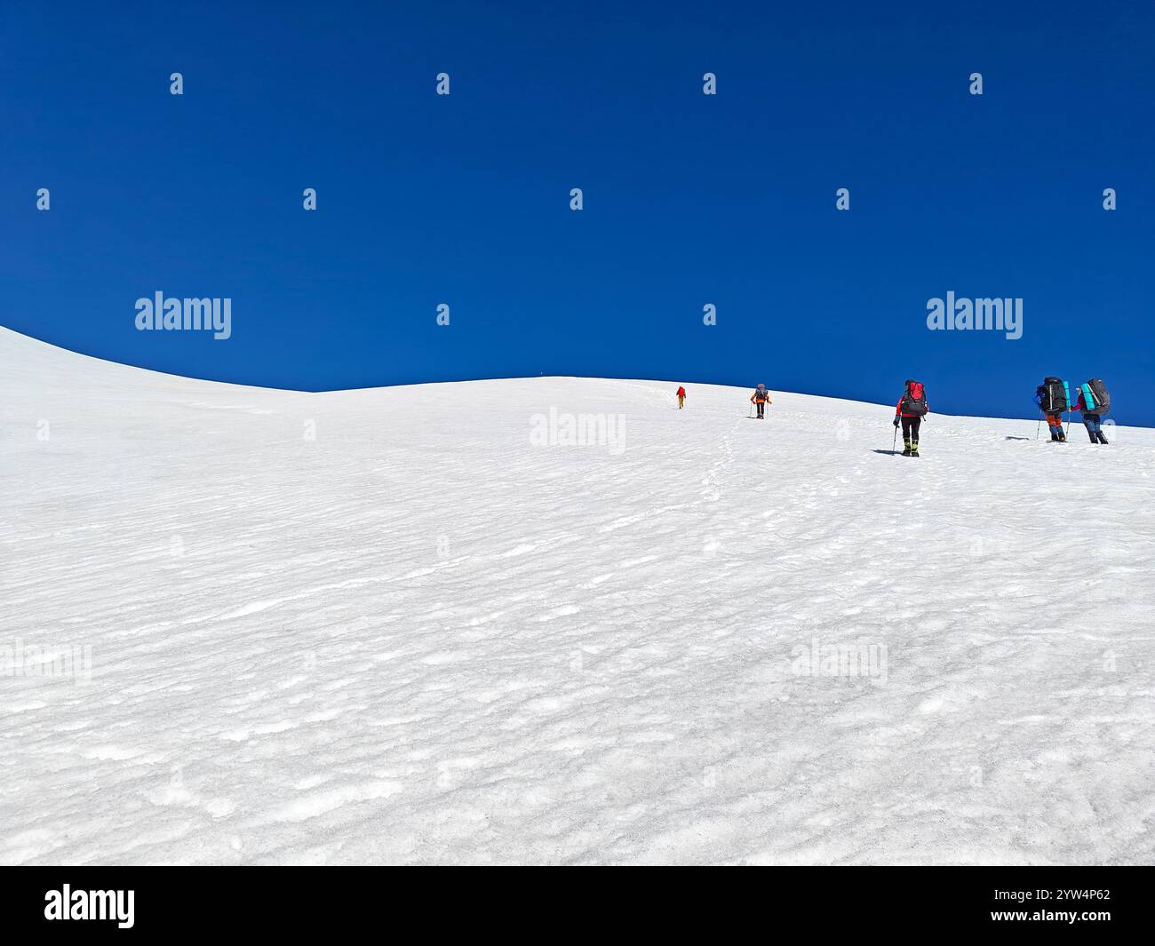 Groups of people climb a snow-covered slope on a bright day in a remote ...