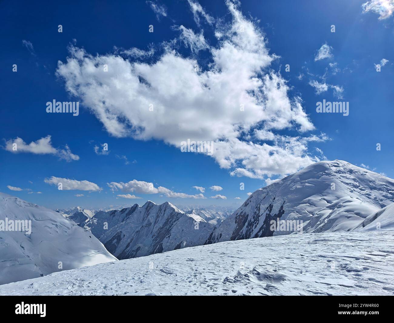 Snow glistens on mountain peaks while fluffy clouds drift across a ...