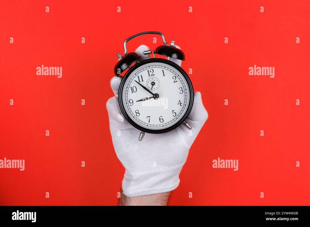 A white-gloved hand holds a classic black alarm clock against a bold ...
