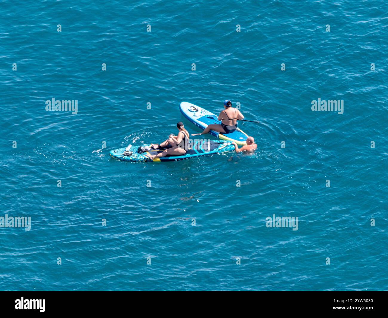 Two women in the sea sitting on SUP boards with paddles Stock Photo - Alamy