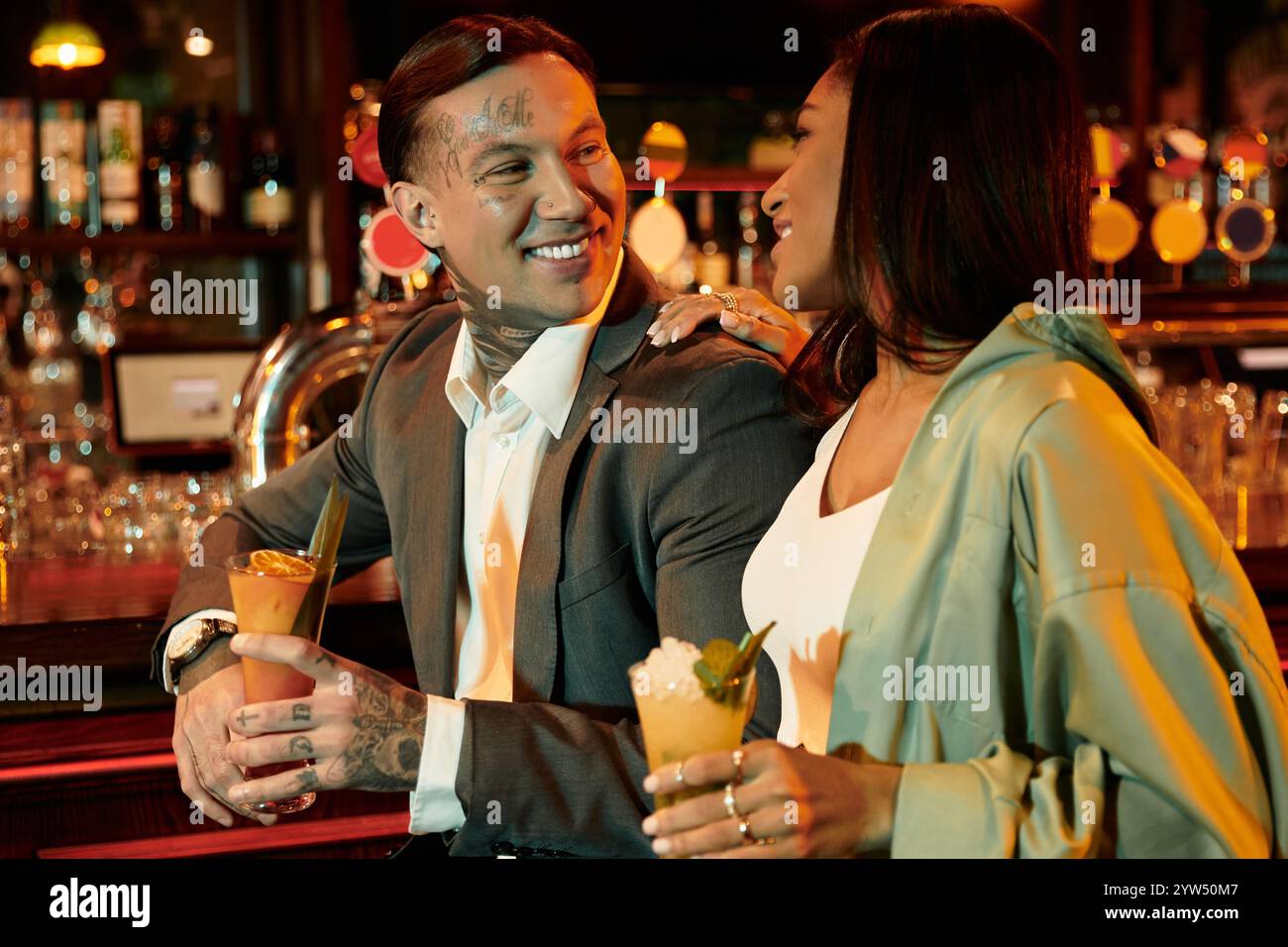 A young couple enjoys cocktails and each others company at a lively bar ...