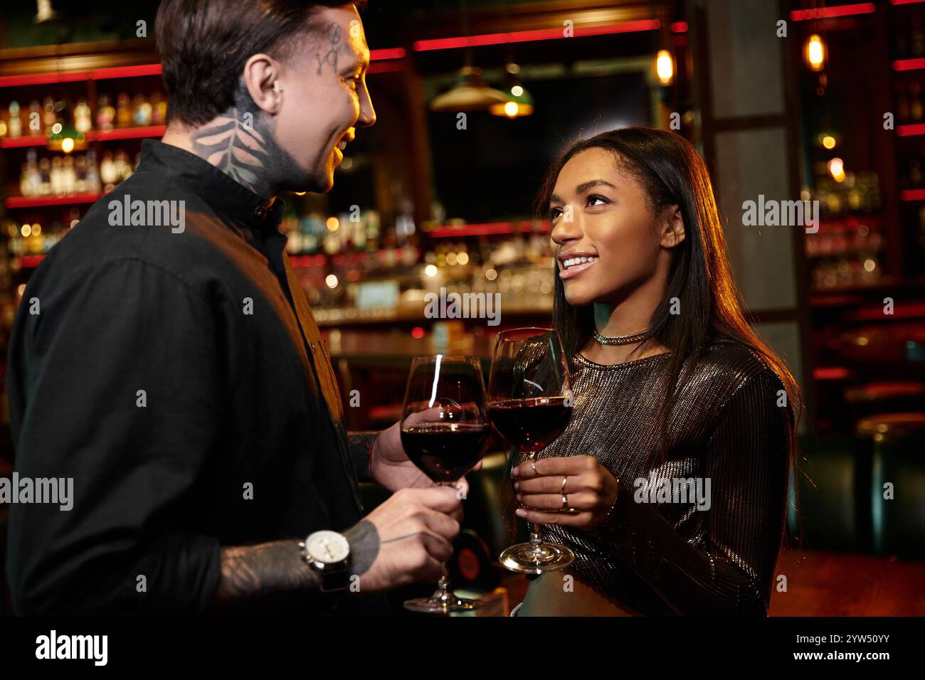 A young couple shares smiles and clinks their glasses in a vibrant bar ...