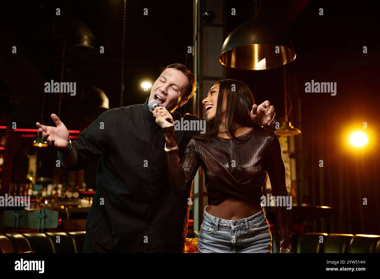 Young couple laughs and sings together, embracing the fun of a karaoke ...