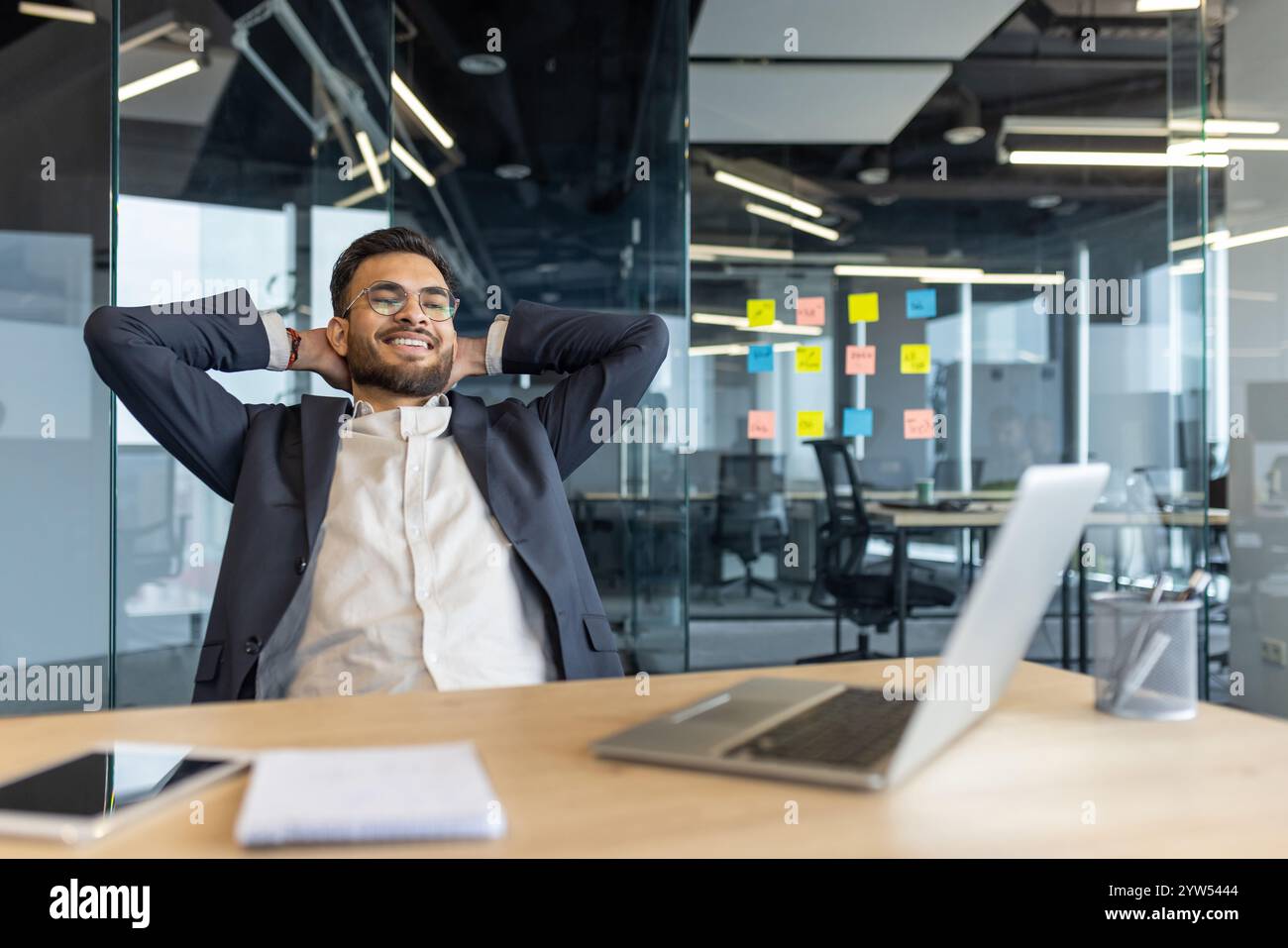 A smiling businessman leans back, feeling relaxed at his desk in a ...