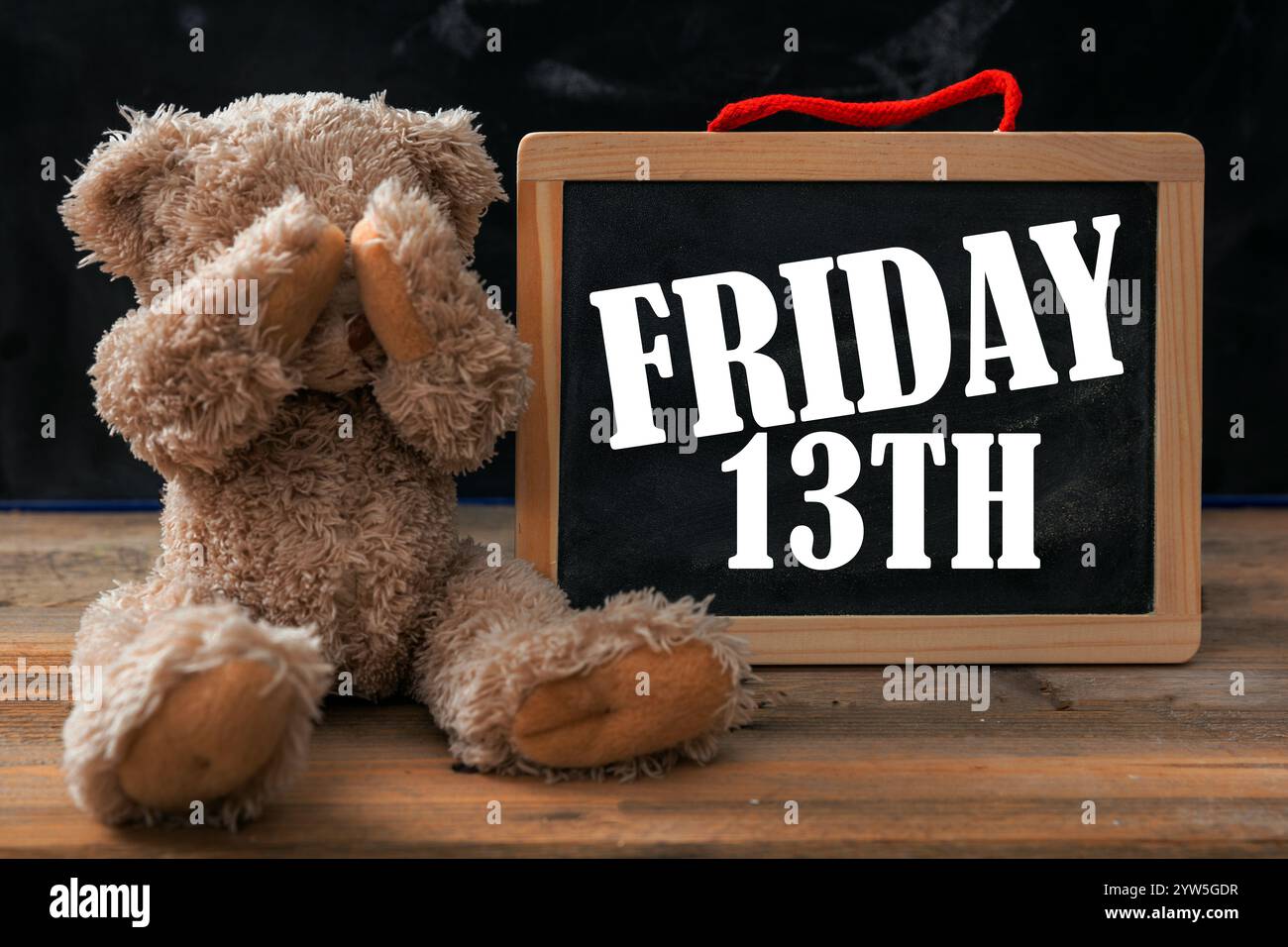 Friday the 13th text on a blackboard, Teddy bear frightened, covering ...