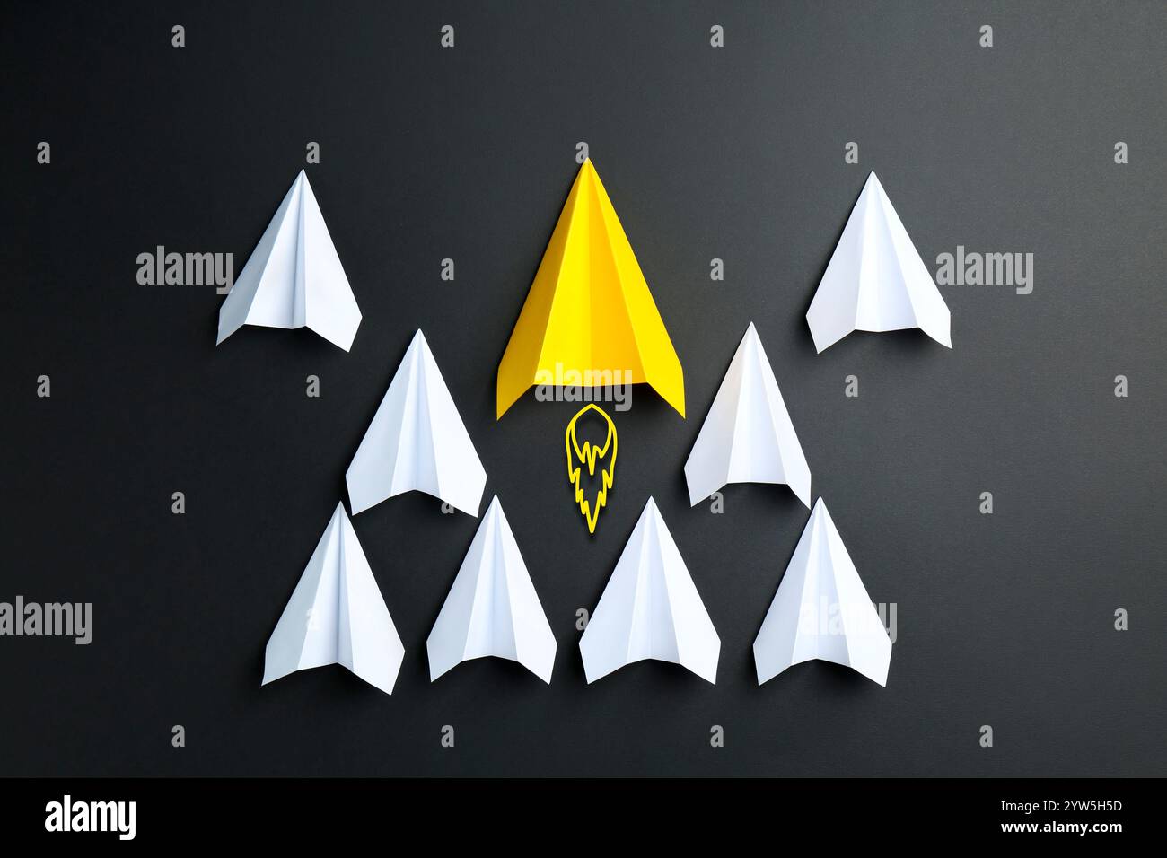 Yellow paper plane bursting forward among white ones on black ...