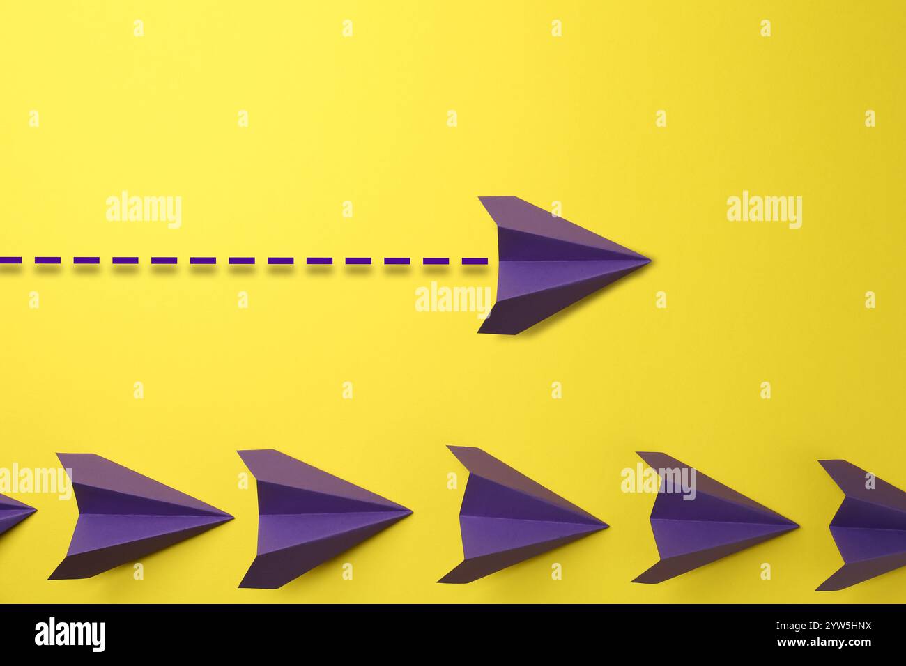 One purple paper plane with flight path over others on yellow ...