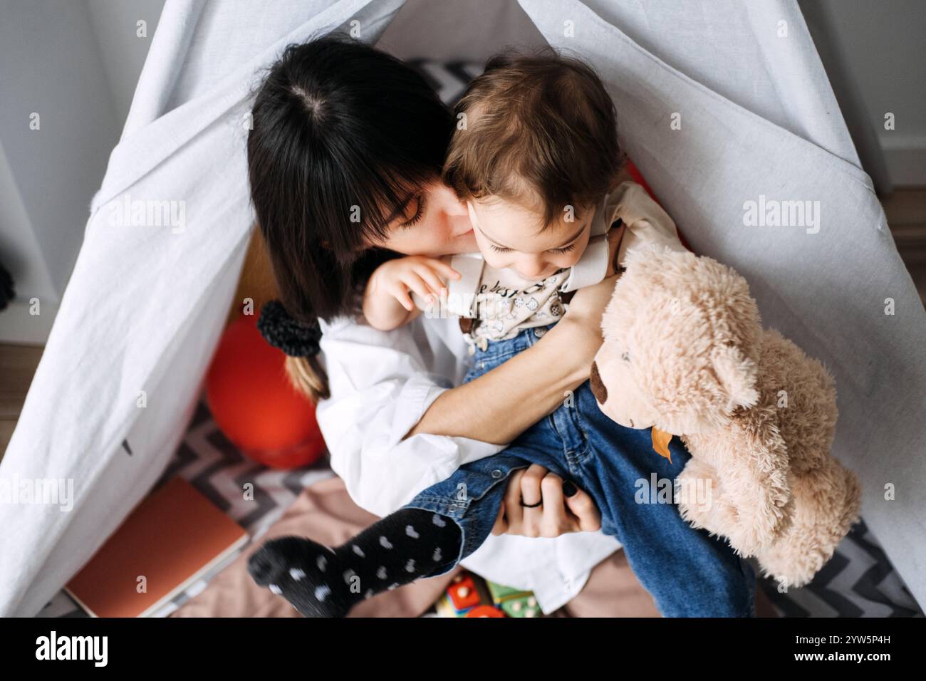 Mother playing with toddler using a toy bear in an indoor tent. Parent ...