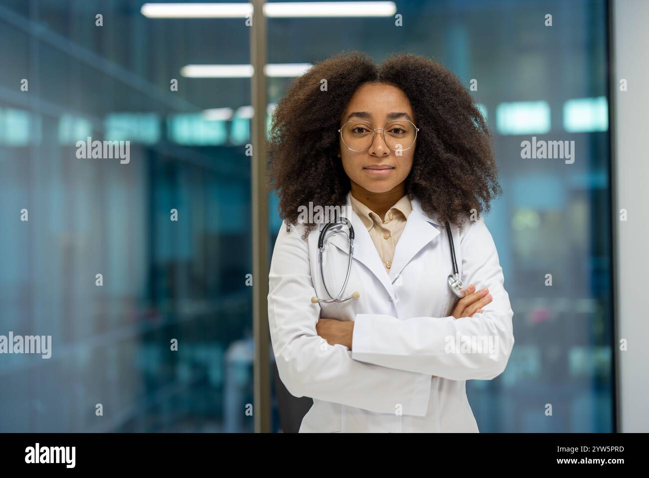 A confident female doctor stands in a hospital corridor, arms folded ...