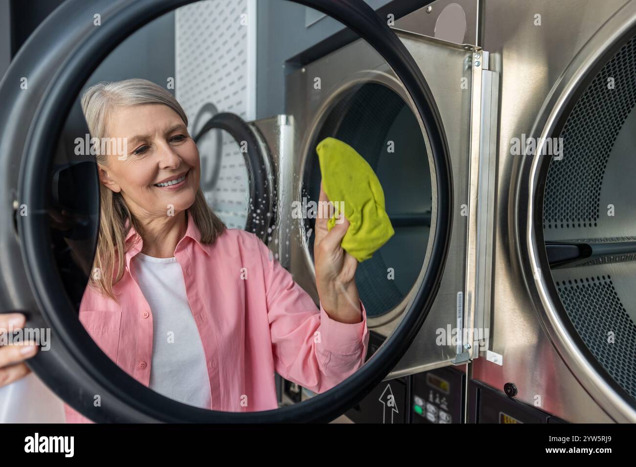 Mature caucasian woman cleaning the washing machine and looking ...