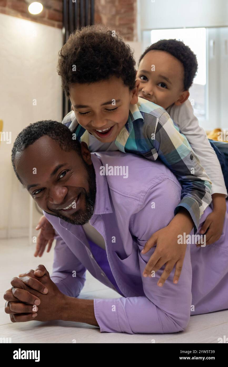 Dark-skinned father playing with his kids and carrying them on his back ...