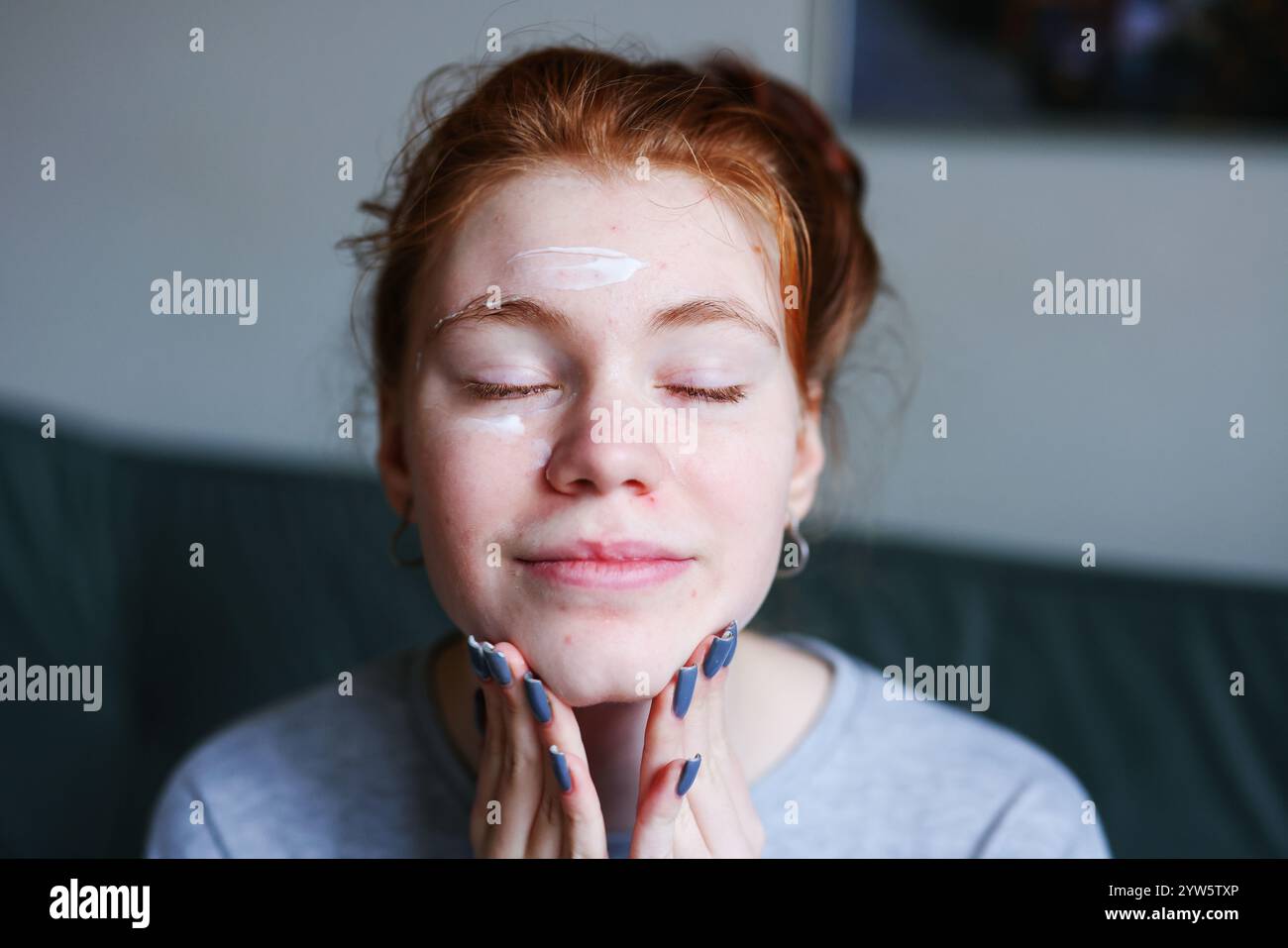 Girl caring of her beautiful skin on the face. Applying moisturizer on ...