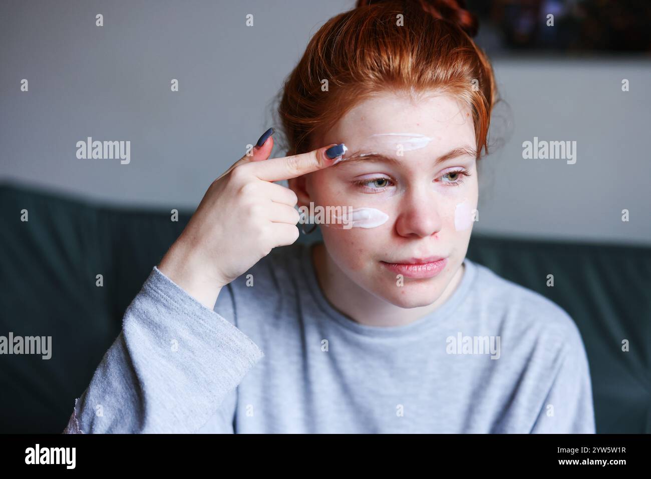 Girl caring of her beautiful skin on the face. Applying moisturizer on ...