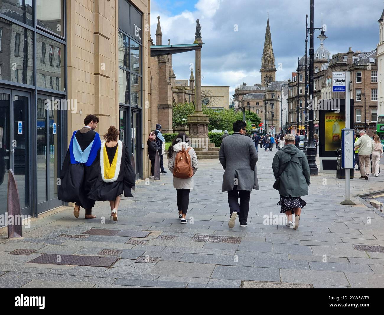 Two college students in graduation gowns (academic regalia) walking on ...
