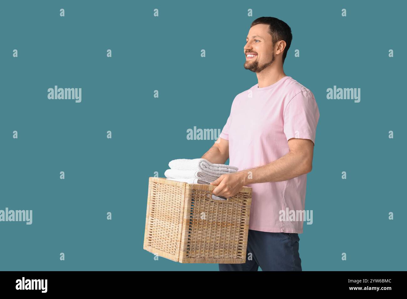 Young man with laundry basket and stack of clean clothes on blue ...