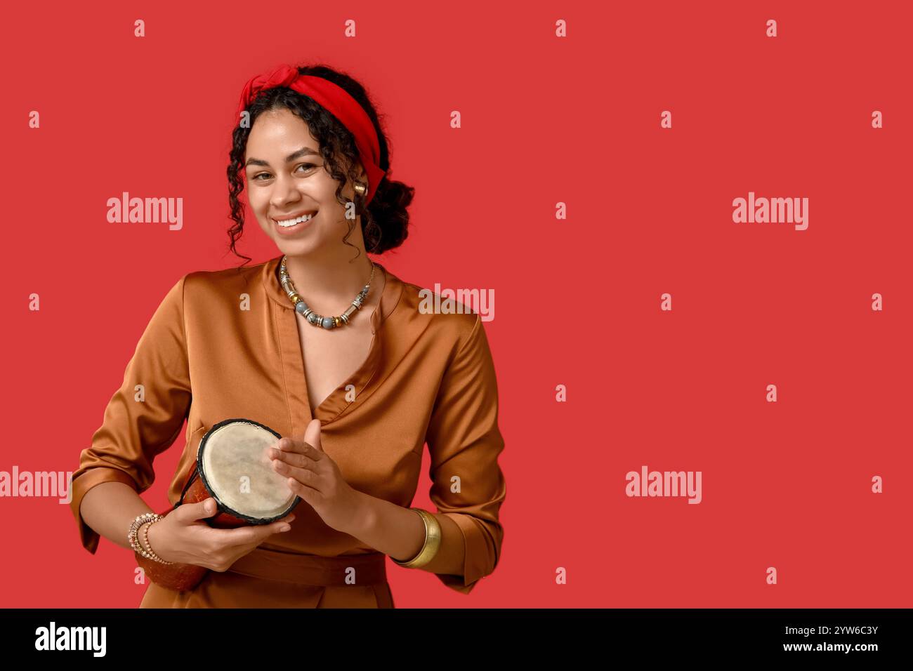 Young African-American woman playing tam-tam drum on red background ...