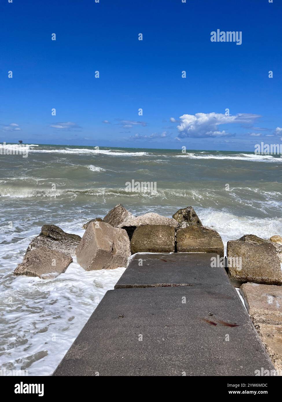 A concrete pier stretches towards the ocean as waves crash against ...