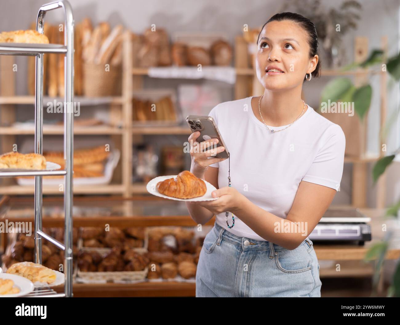 Middle-aged woman stands in bakery, scanning croissant with her phone ...