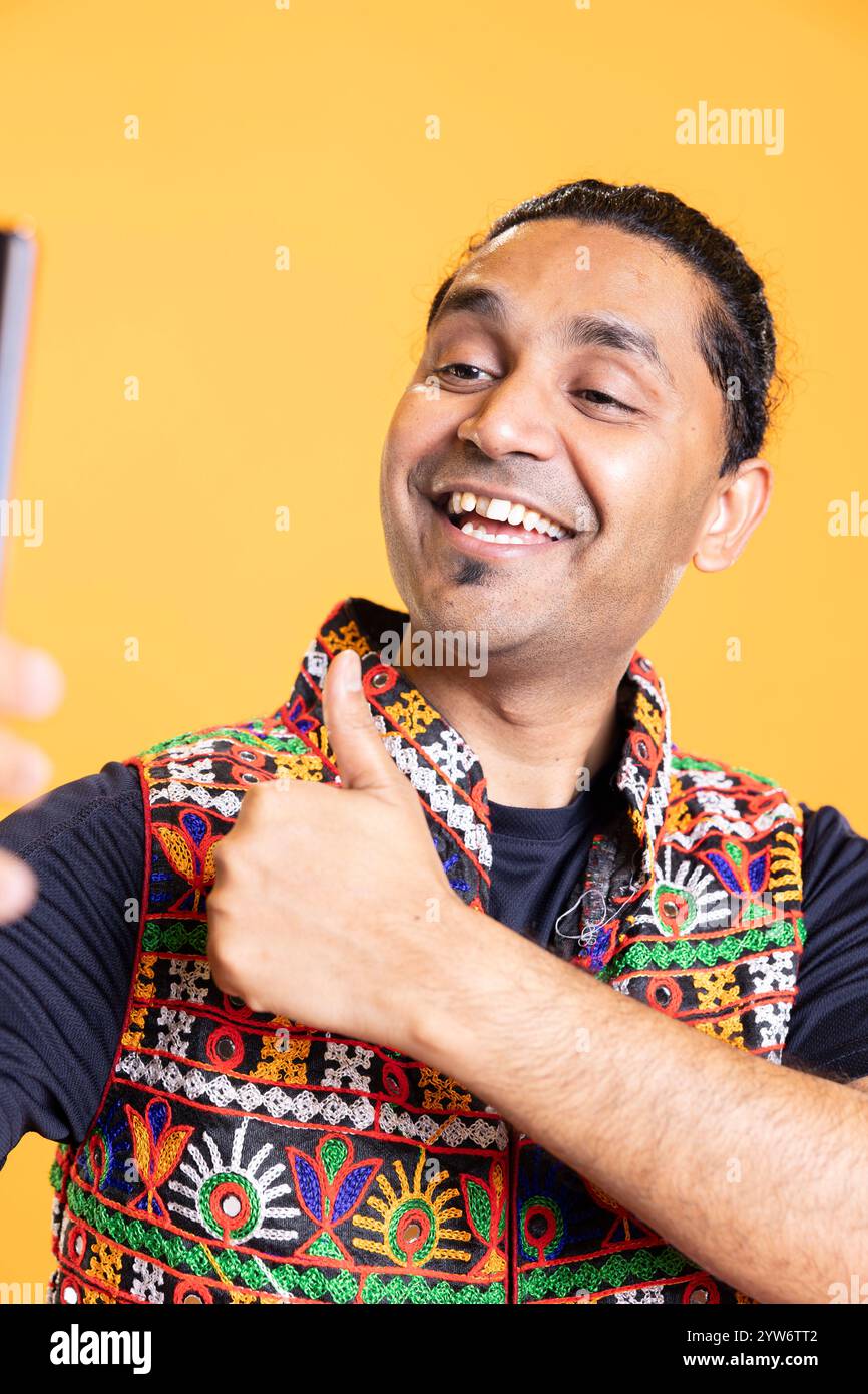 Happy man using cellphone to take selfies, doing thumbs up gesture. Jolly social media user ...