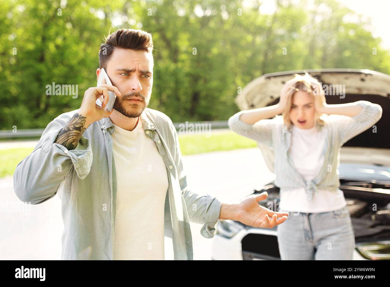 Young guy standing near broken car together with terrified girlfriend ...