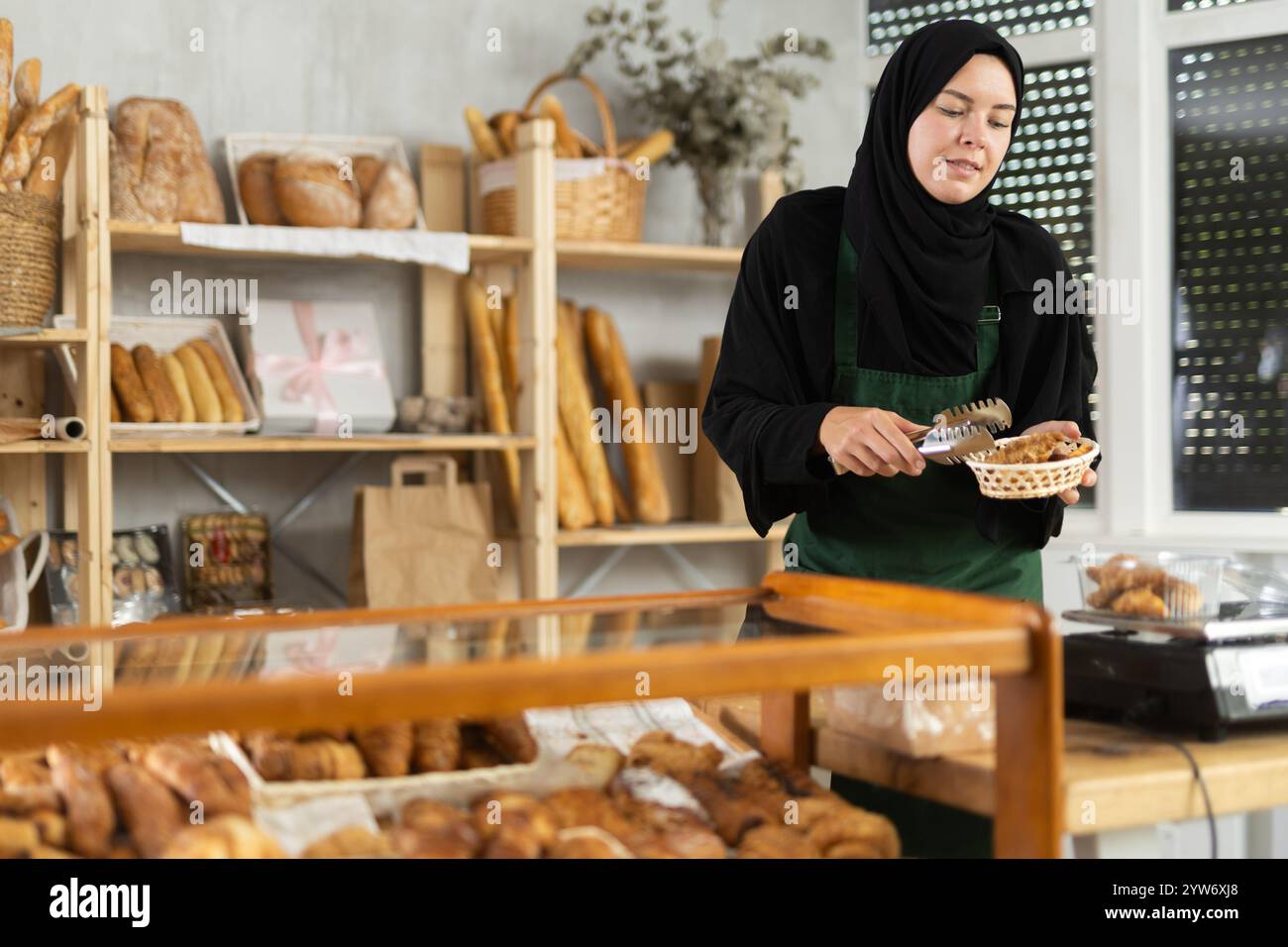 European Muslim woman seller in hijab weighs croissants on scale Stock ...