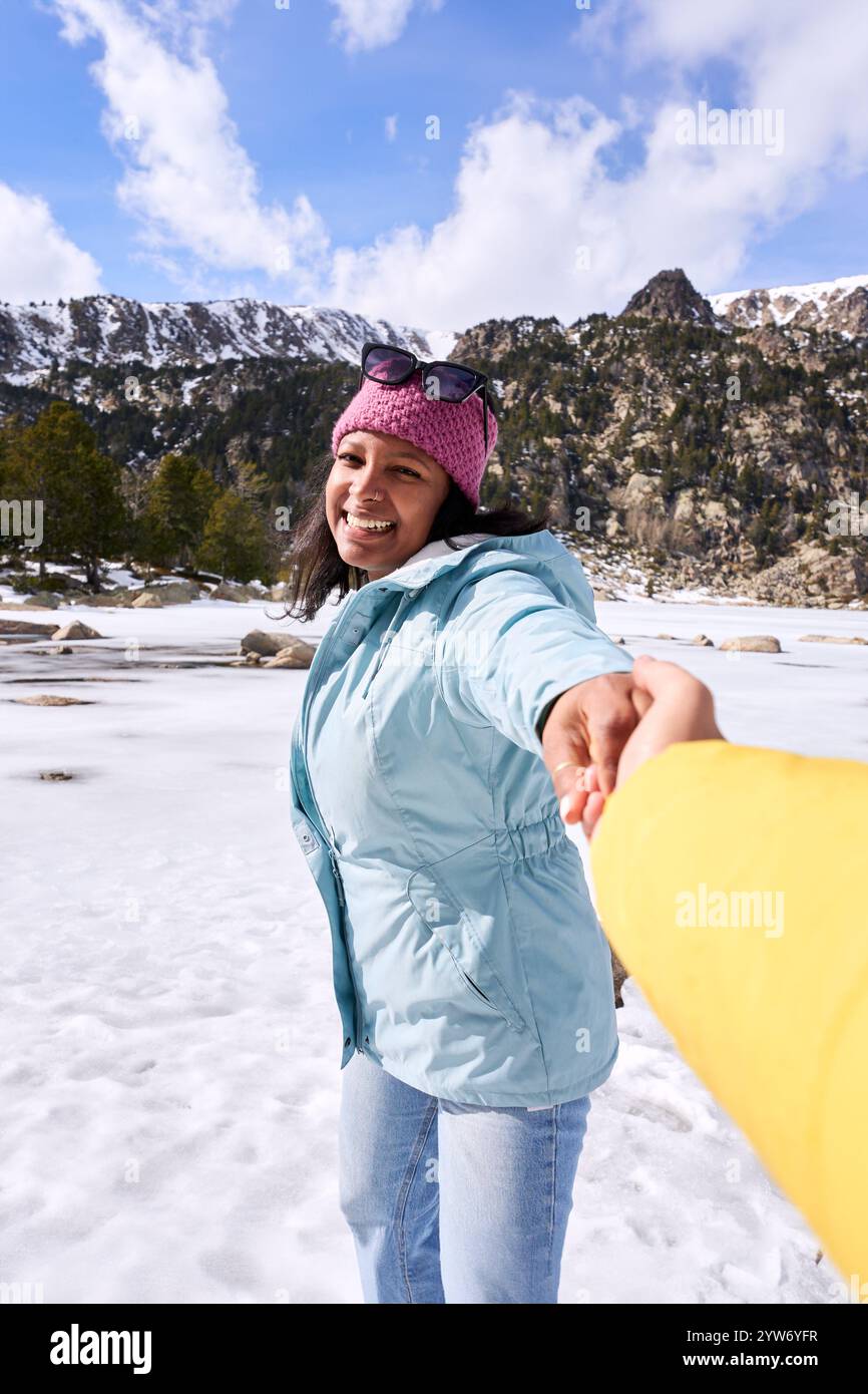 Happy woman guiding her partner through snowy forest, holding his hand ...