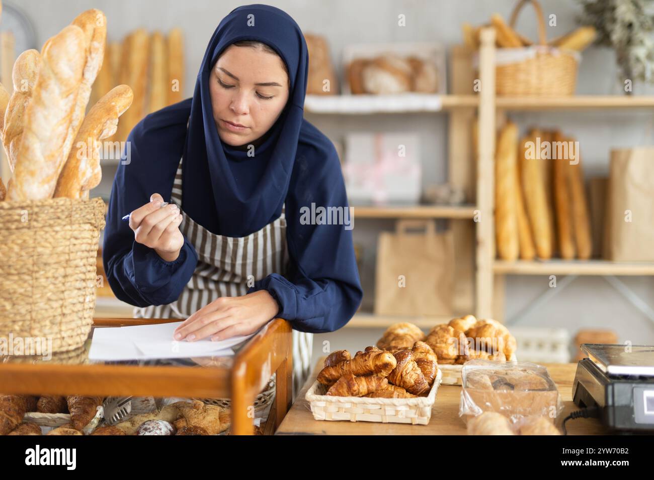 European woman in hijab reviewing paperwork while managing bakery Stock ...