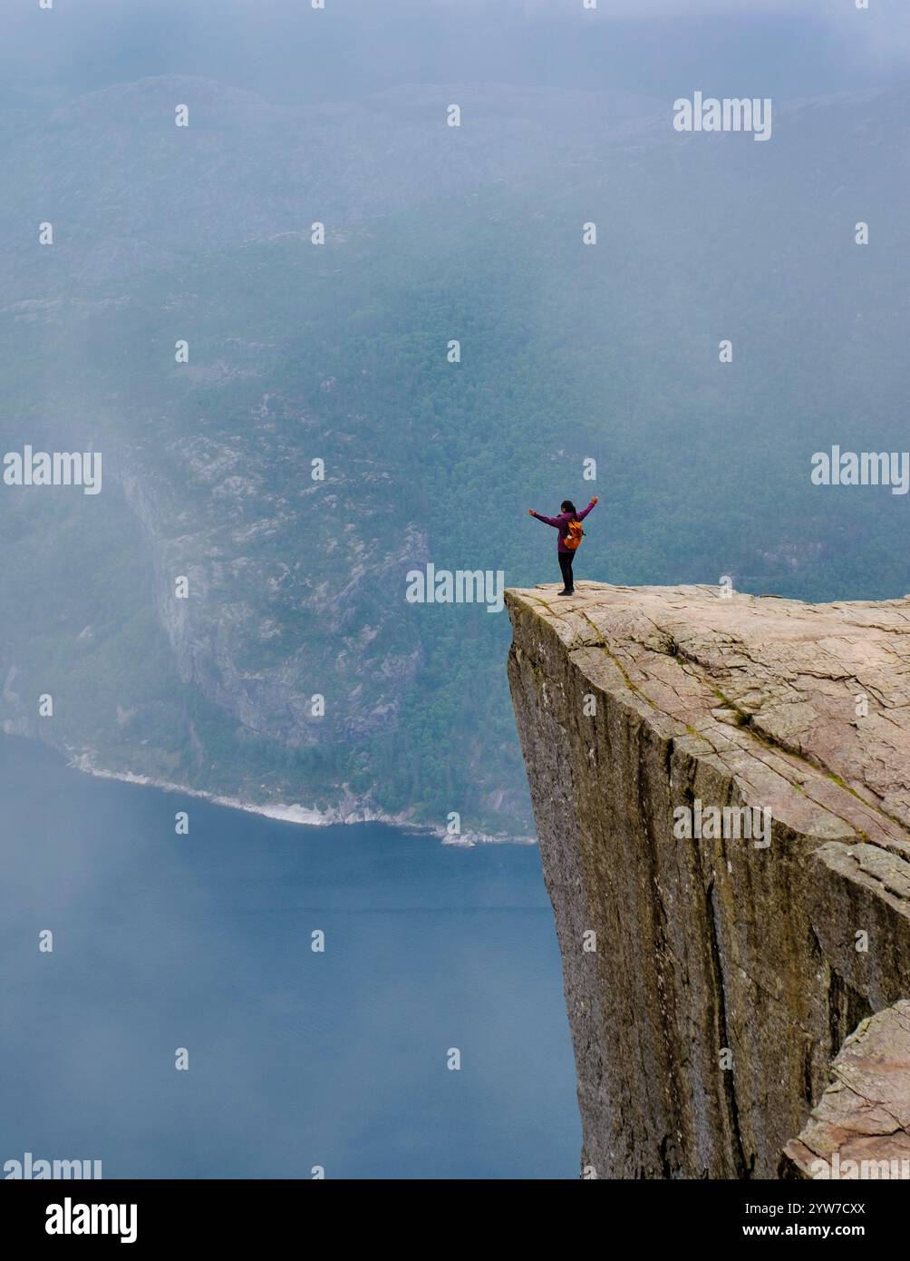A hiker stands on the edge of a cliff with arms outstretched, taking in ...
