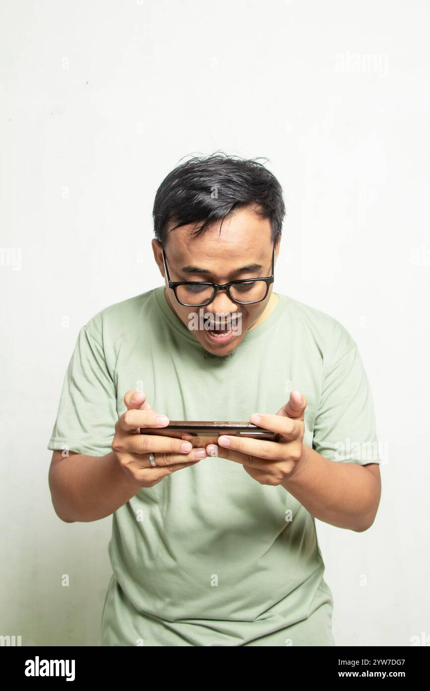Asian Indonesian bespectacled man surprised while playing mobile game ...