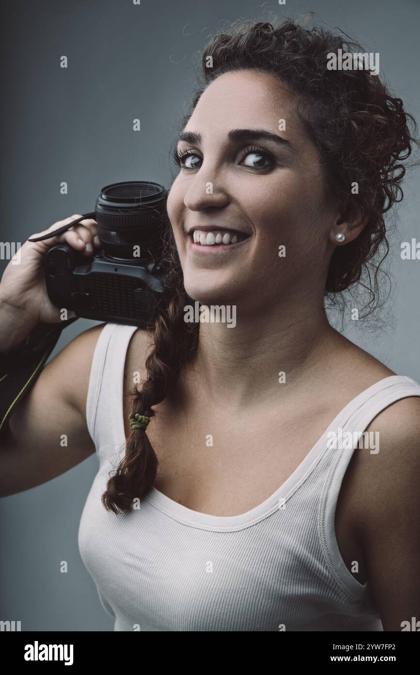 Cheerful young woman photographer holding a dslr camera on her shoulder ...
