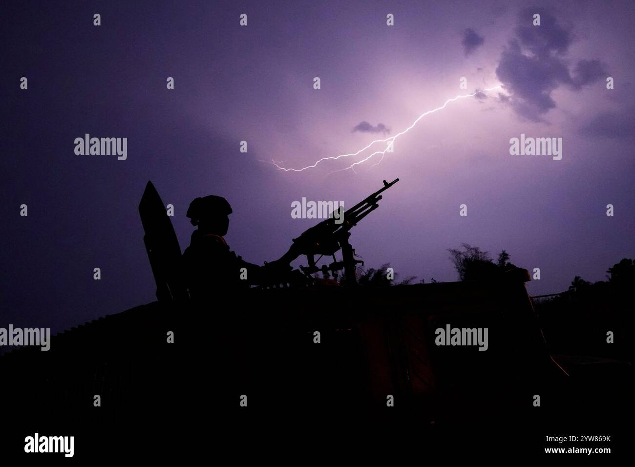 Lightning illuminates the sky behind the gunner on a Thai military ...