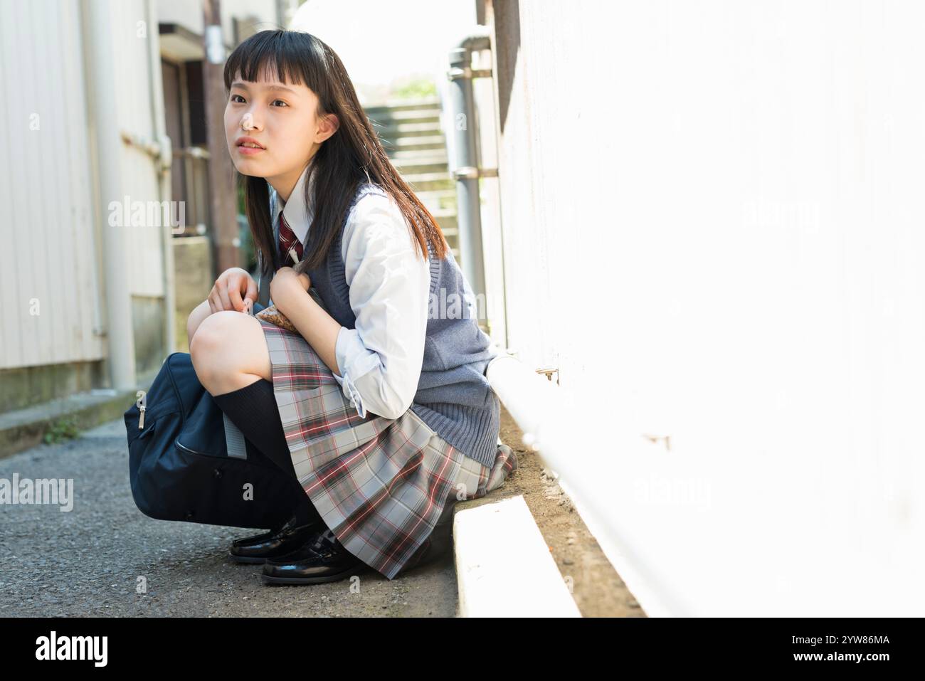 Female high school student crouching down on the way to school Stock ...