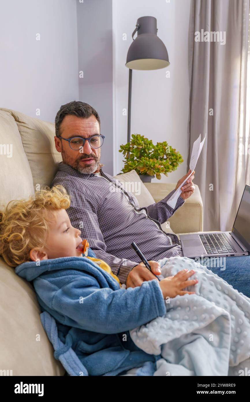 Father working remotely while caring for his toddler son, balancing ...