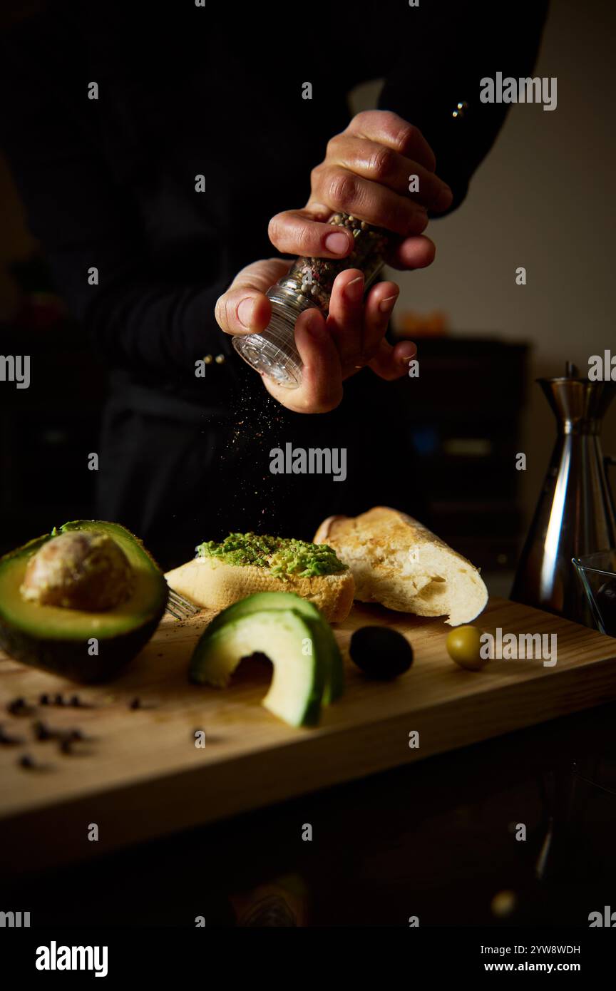 Close-up of a hand seasoning avocado toast with pepper, highlighting ...