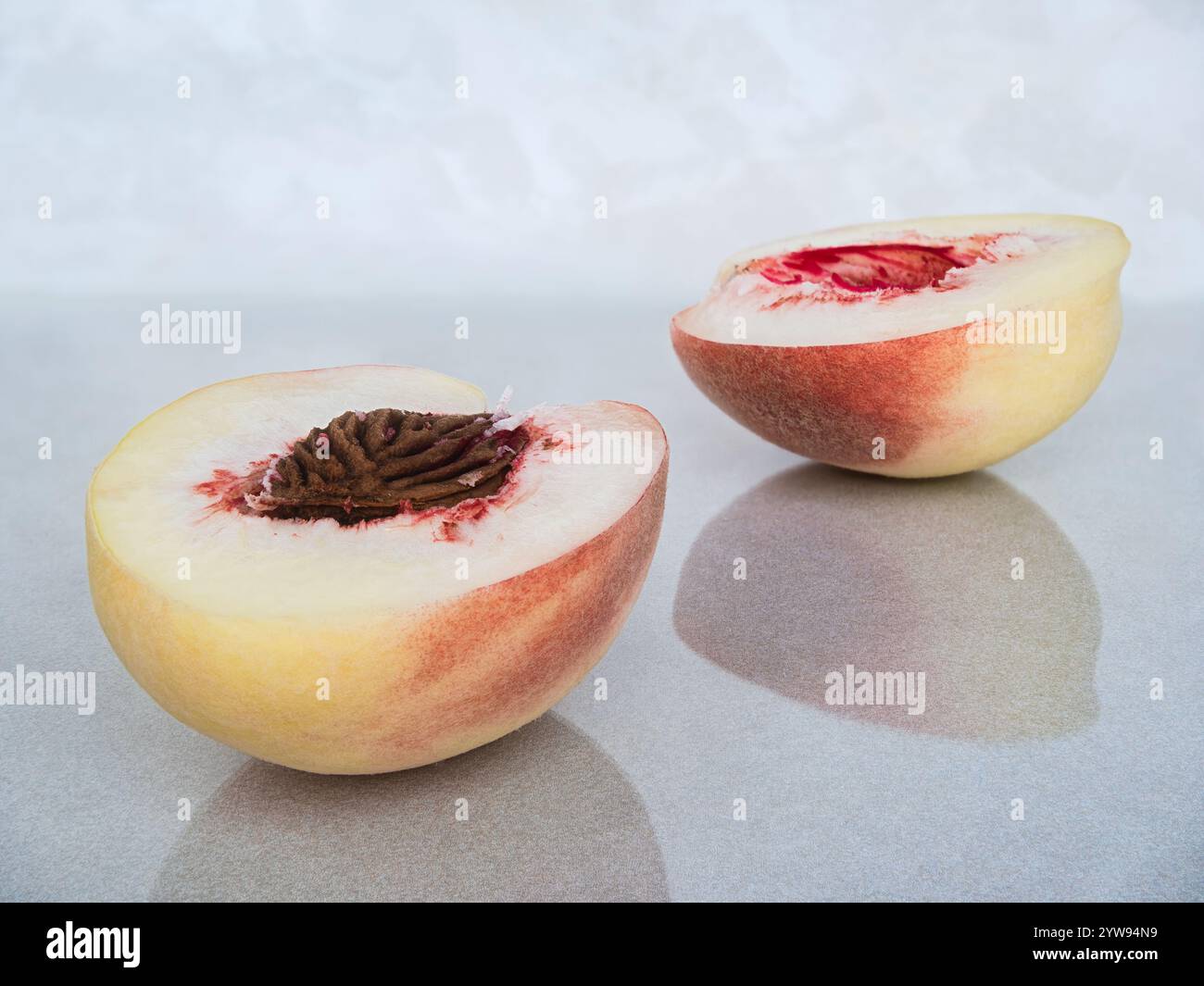 White Swan peach split in half on polished surface with reflection ...