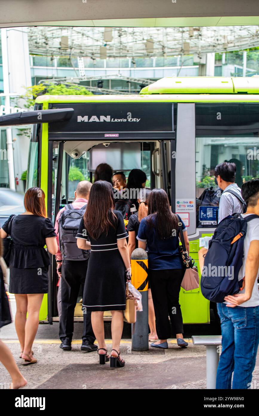 Weekday commuters wait to join a yellow bus at a bus stop in central ...
