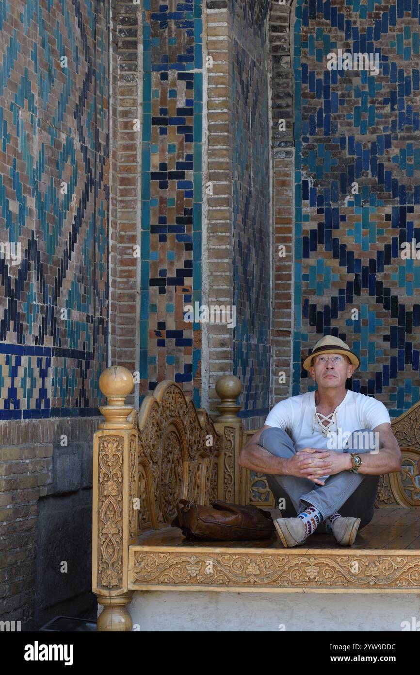 Tourist man sitting on bench in inner courtyard of Tilya-Kori Madrasah ...
