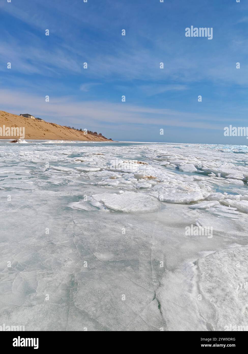 Frozen ice stretches across the water towards sandy hills under a ...