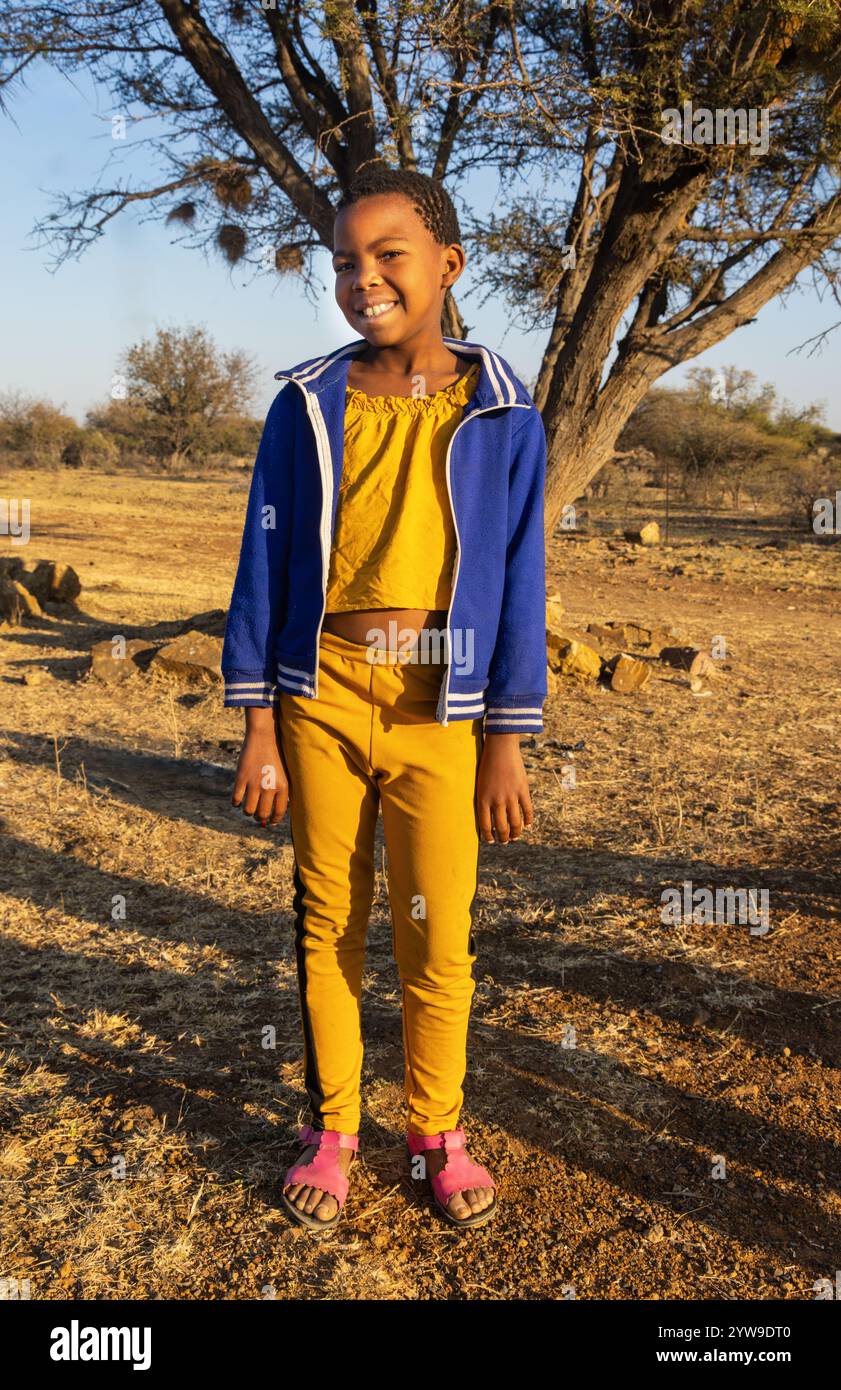 village portrait of single african child outdoors, tree and bush in the ...