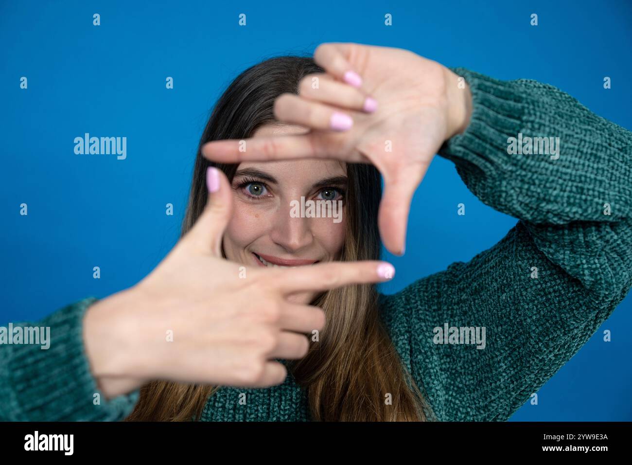 Smiling woman framing her face with hands, expressing creativity and ...